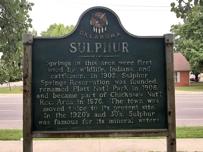 History speaks through this weathered green sign, telling tales of mineral springs that drew wildlife, Native Americans, and eventually created a town that moved—twice!—for its magical waters.
