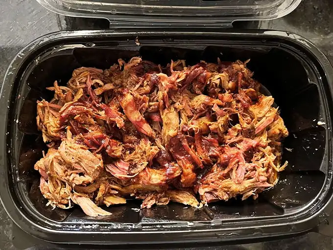 Pulled pork in its natural habitat—ready for the journey home. This container holds enough smoky treasure to make your kitchen smell like heaven.