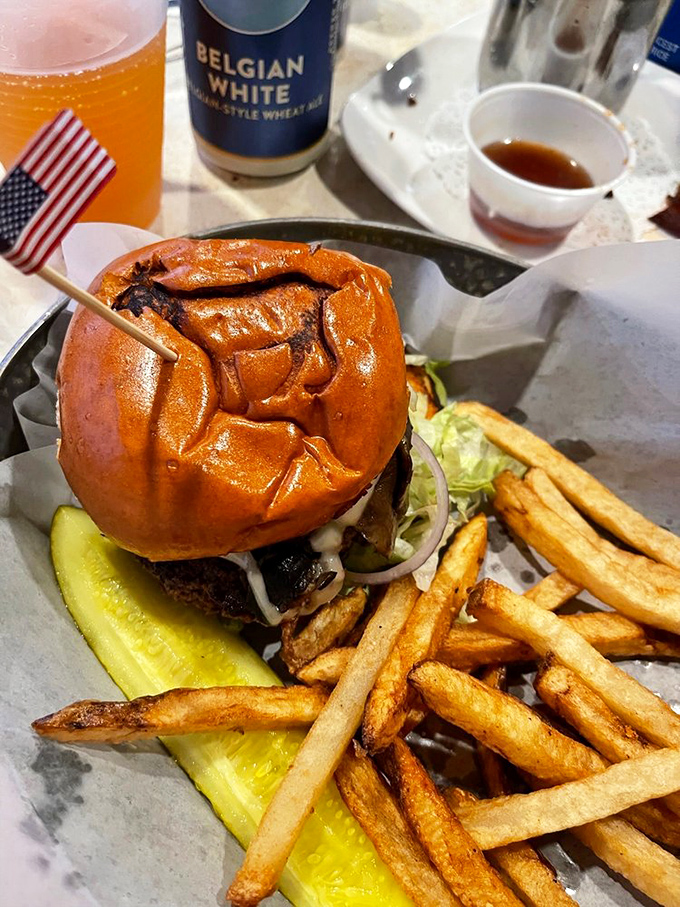 This isn't just a burger—it's an architectural marvel with a pickle foundation and golden fry buttresses. The American flag toothpick claims this territory for deliciousness.