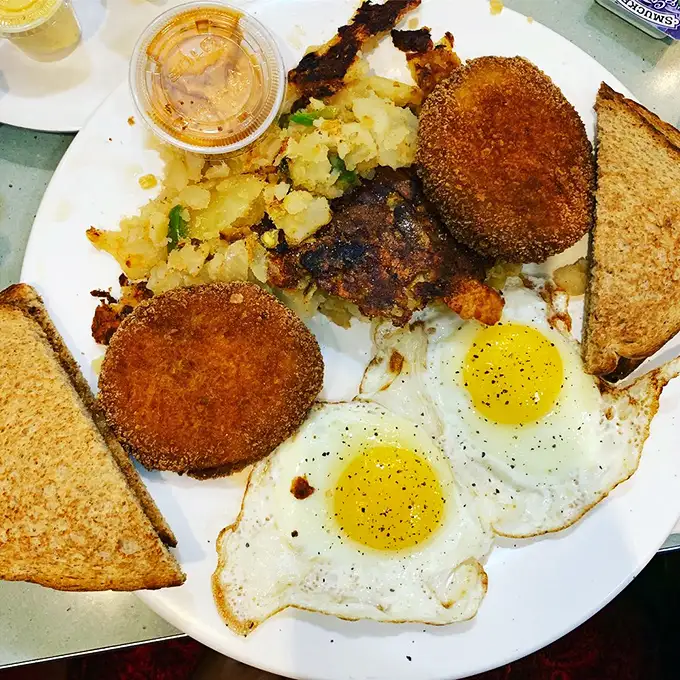 Golden crab cakes and sunny-side up eggs sharing a plate like old friends, with home fries playing matchmaker. Breakfast democracy at its finest.