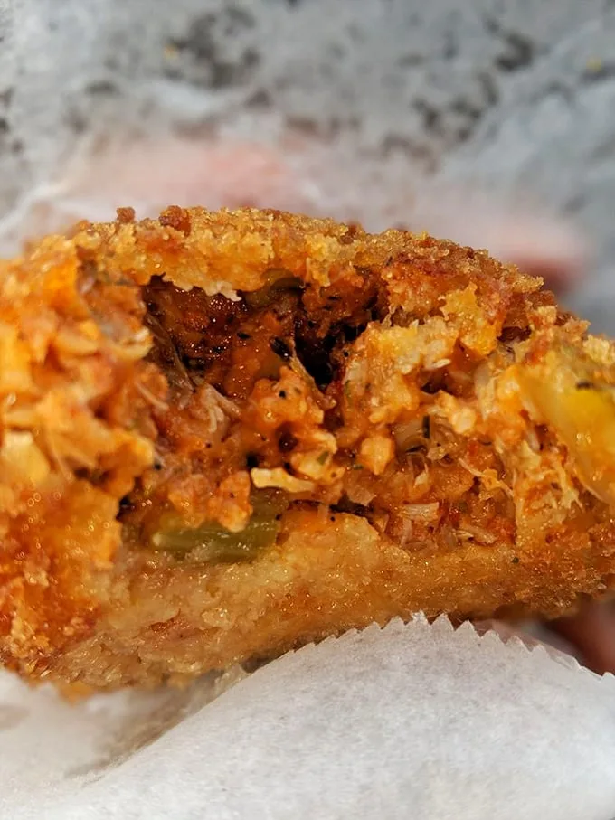 Behold the star attraction—deviled crab with a golden crust that shatters like delicate glass, revealing spiced treasure within. Food poetry in football form.