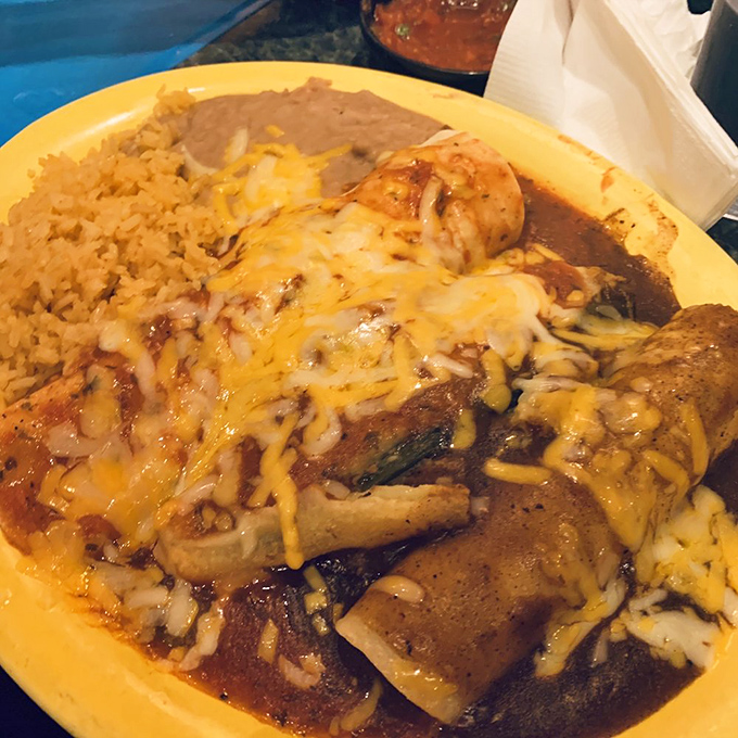 Cheese-blanketed enchiladas arrive like a warm hug on a plate, surrounded by perfectly cooked rice and beans that refuse to be mere sidekicks.