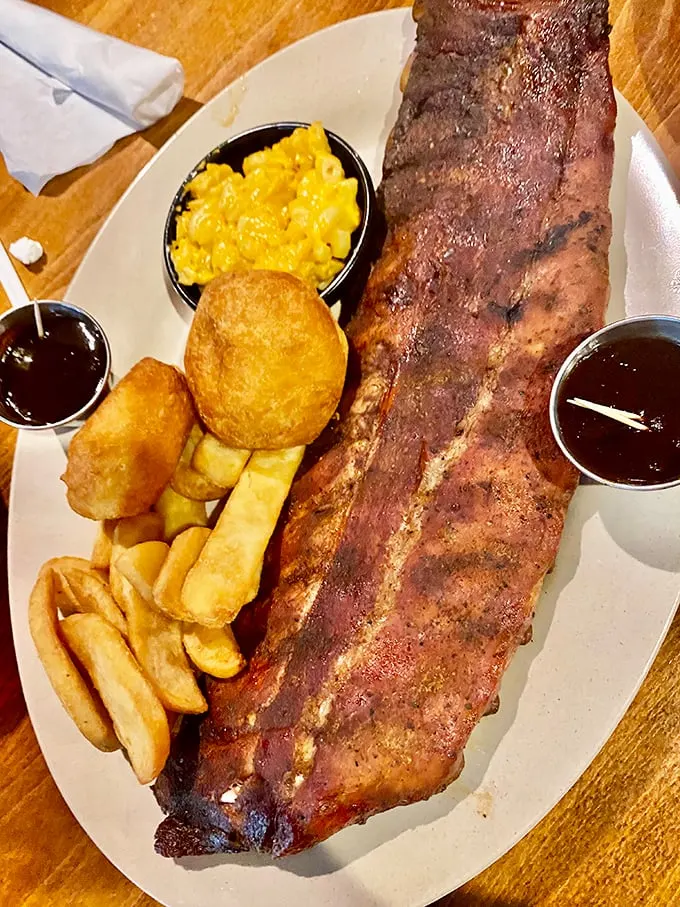 Behold the rack of ribs in its natural habitat—surrounded by mac and cheese, fries, and two dipping sauces for strategic flavor deployment.