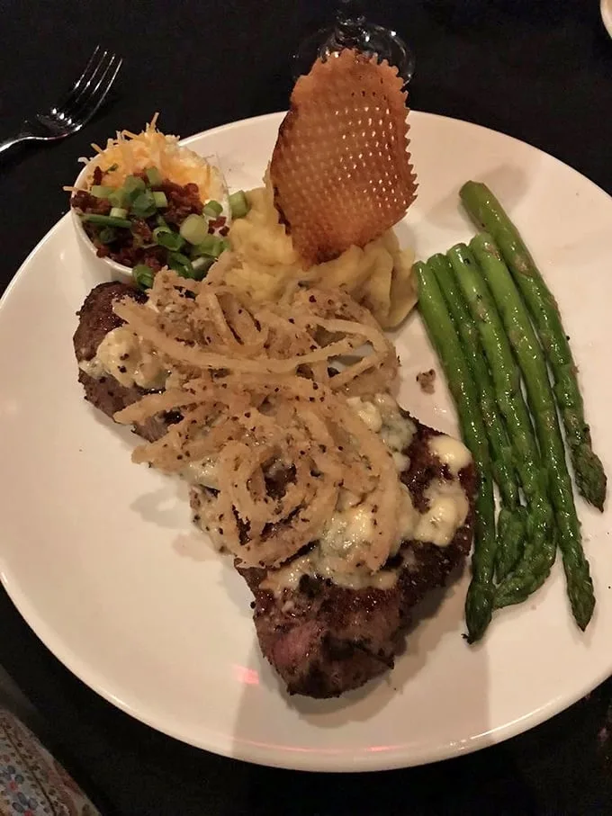This isn't just steak—it's a masterpiece with crispy onion strings and perfect sides. The kind of plate that makes conversation stop mid-sentence.