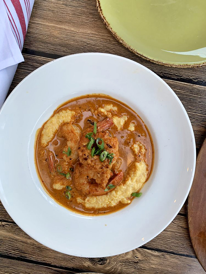 The legendary shrimp and grits in their natural habitat—a pristine white bowl where plump shrimp and creamy grits perform a culinary tango.