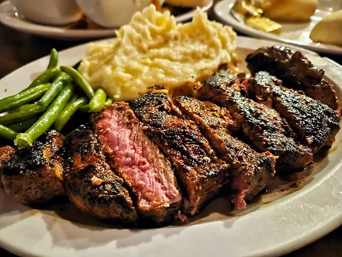 The medium-rare ribeye arrives like edible artwork—charred exterior giving way to a ruby center, flanked by creamy mashed potatoes and vibrant green beans.