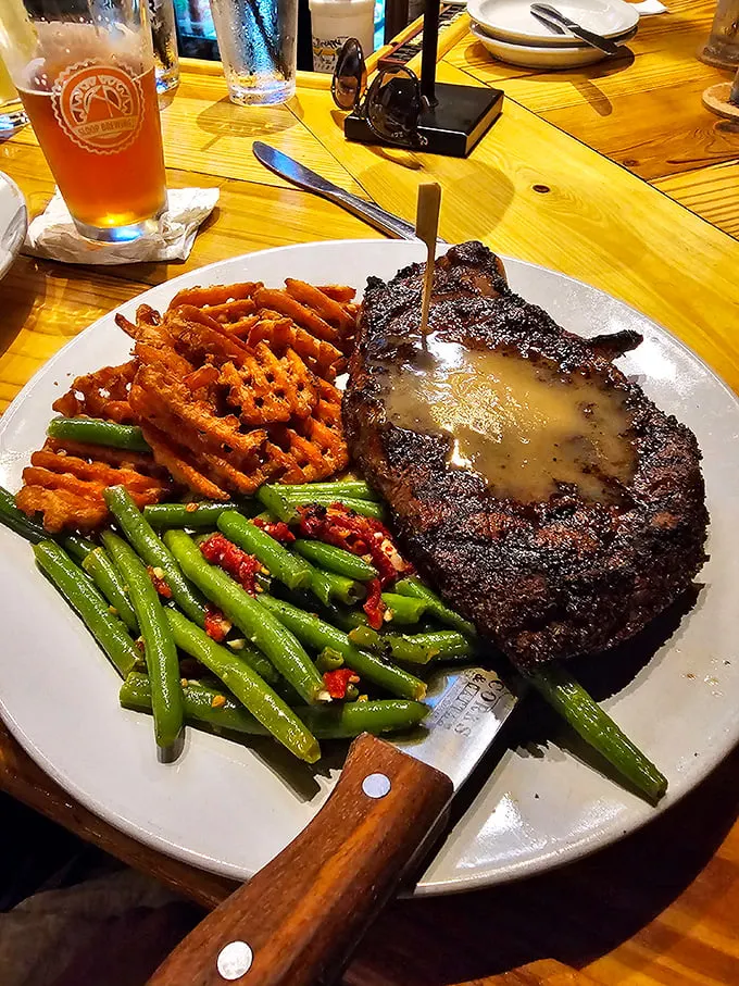 The steak doesn't just sit on the plate—it commands attention like Pavarotti on stage, with sweet potato waffle fries playing backup.