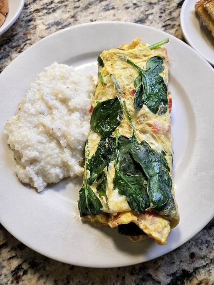 The spinach omelet doesn't just arrive on your plate—it makes an entrance, all fluffy and proud, with grits standing by as the perfect supporting actor.