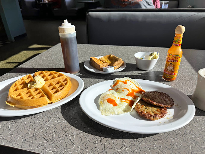 Breakfast perfection on a plate – golden waffles with a pat of melting butter alongside eggs and sausage. This is how mornings were meant to begin.