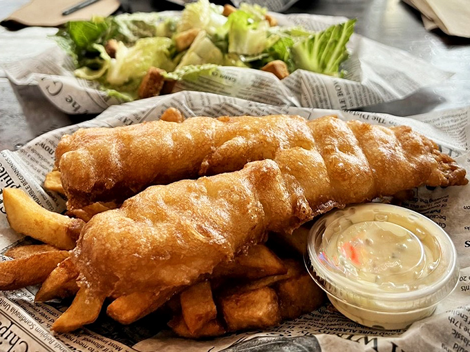 Golden-battered fish resting on a bed of thick-cut chips. This isn't just fried food—it's edible sunshine wrapped in newspaper.