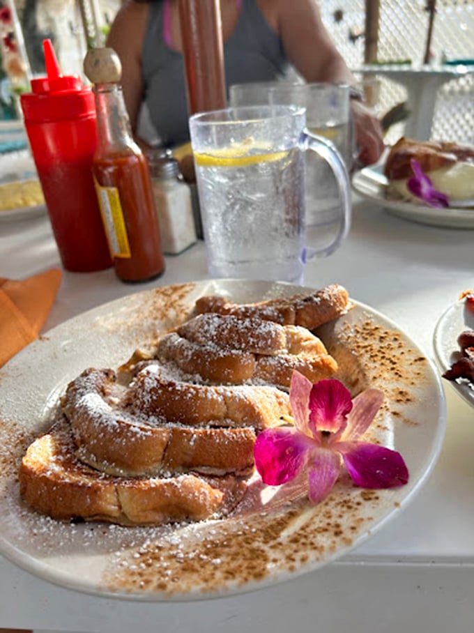 This French toast doesn't just arrive at your table—it makes an entrance, dusted with powdered sugar and adorned with an orchid like it's headed to a tropical gala.