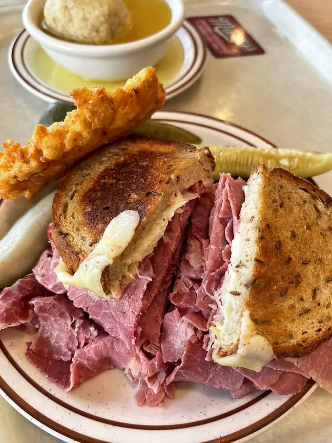 The Reuben in its natural habitat, flanked by matzo ball soup and a potato pancake—the holy trinity of deli comfort.