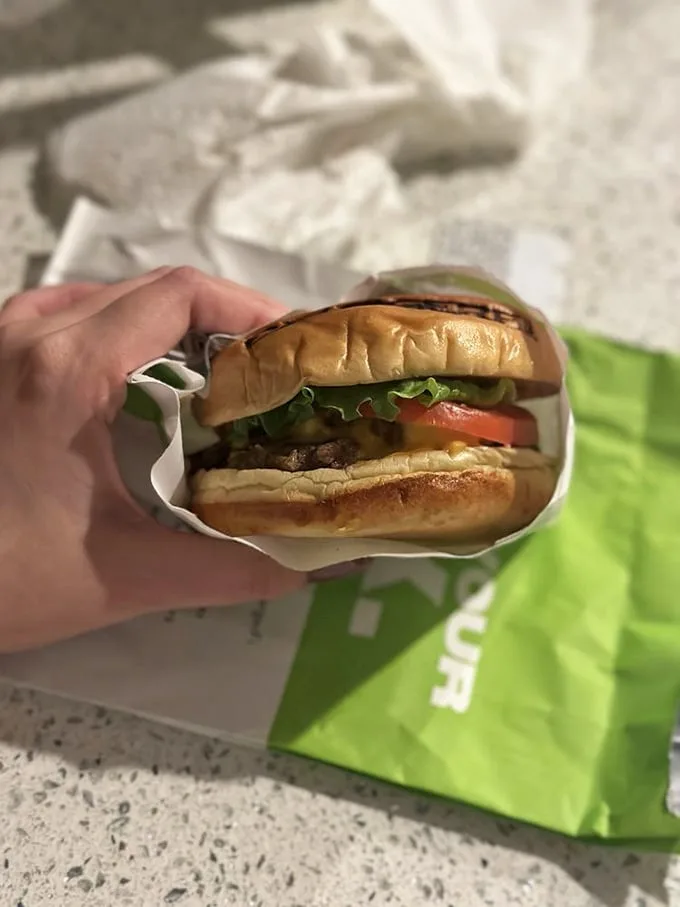 Behold the perfect burger cross-section: juicy patty, melty cheese, fresh veggies, and a bun that's somehow both sturdy and tender—architectural perfection in food form.