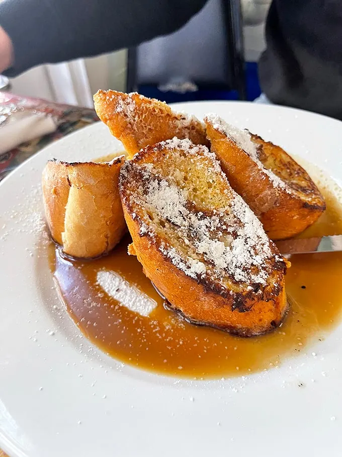 Pain Perdu elevated to art form – bread soaked in custard until surrendering completely, then baptized in syrup and powdered sugar for heavenly results.