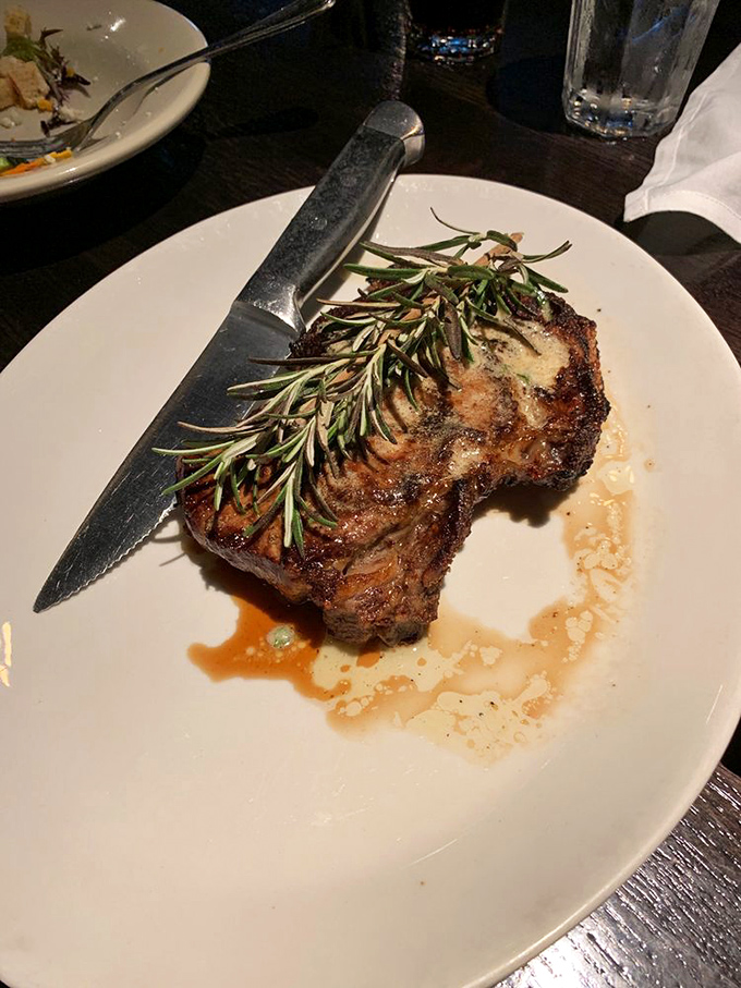 That rosemary sprig isn't just garnish—it's a victory flag planted atop a mountain of perfectly aged beef. The knife stands ready for the expedition.