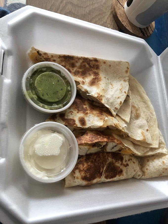 Quesadillas done right—crispy exterior, molten cheese interior, with sides of cool sour cream and that vibrant green sauce for perfect temperature contrast.