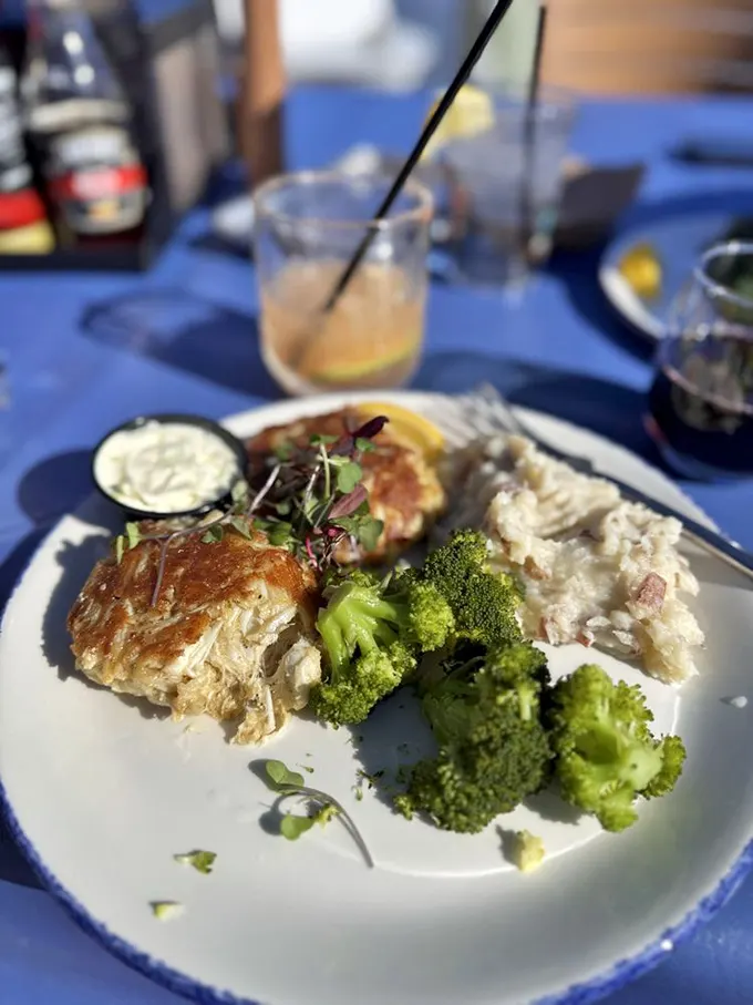 Crabcakes and broccoli bathed in golden sunlight—the kind of plate that makes you pause mid-conversation to admire before diving in.