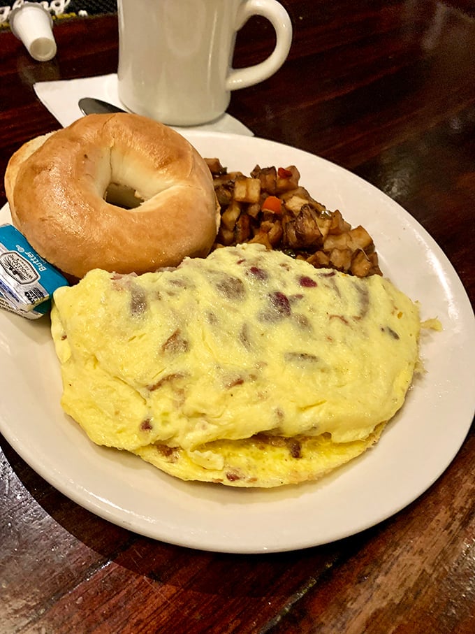 Breakfast diplomacy at its finest – a fluffy omelet stuffed with savory goodness, served with home fries and a bagel for proper morning negotiations.