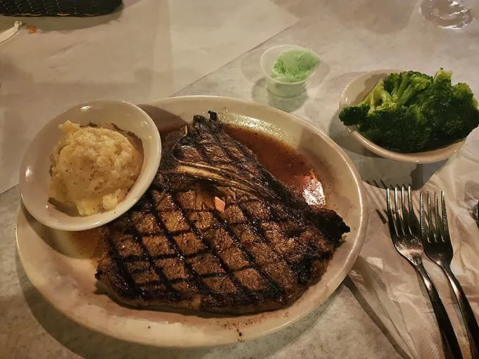 T-bone steak, mashed potatoes, and broccoli: the holy trinity of steakhouse religion, presented with reverence on a simple white plate.