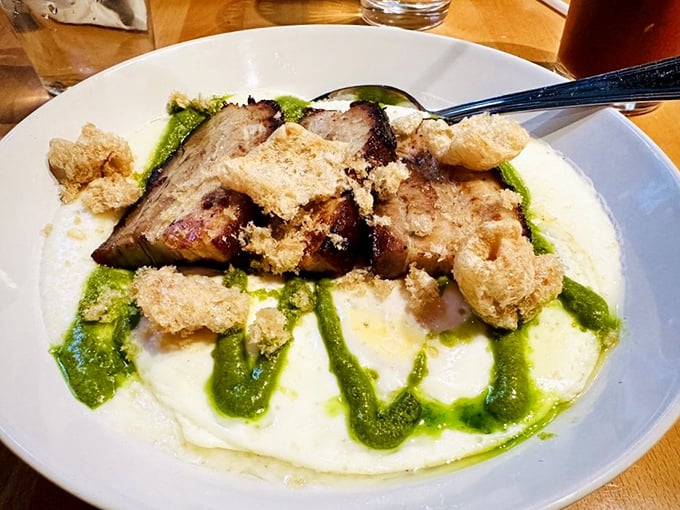 Pork belly resting on a cloud of grits with vibrant green sauce—proof that breakfast can be both comforting and sophisticated, like wearing slippers with a tuxedo.