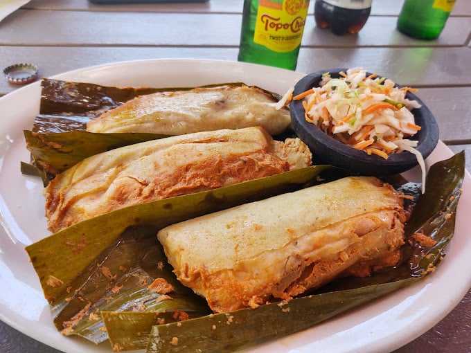 A plate of tamales with curtido and traditional sides – proving that true luxury isn't about white tablecloths but about food that speaks directly to your soul.