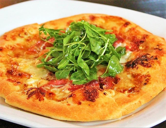Who needs a plane ticket to Italy when this prosciutto pizza exists? The arugula on top isn't just garnish—it's the emerald crown.
