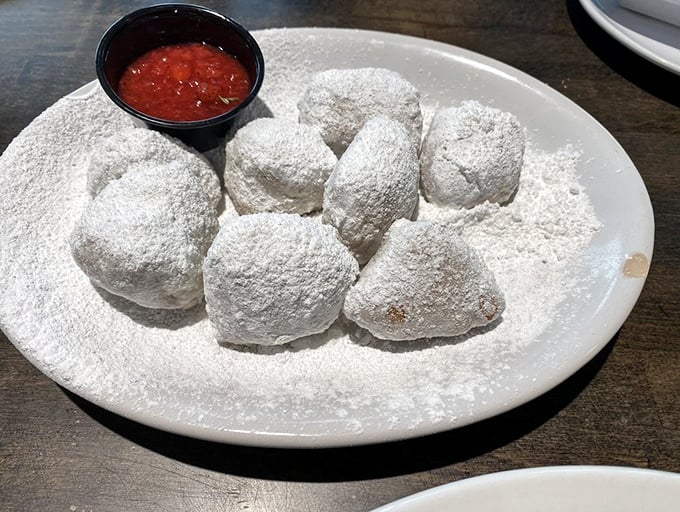 Powdered sugar snowdrifts hiding pillowy beignet treasures. The side of jam adds that perfect sweet-tart counterpoint to these morning indulgences.