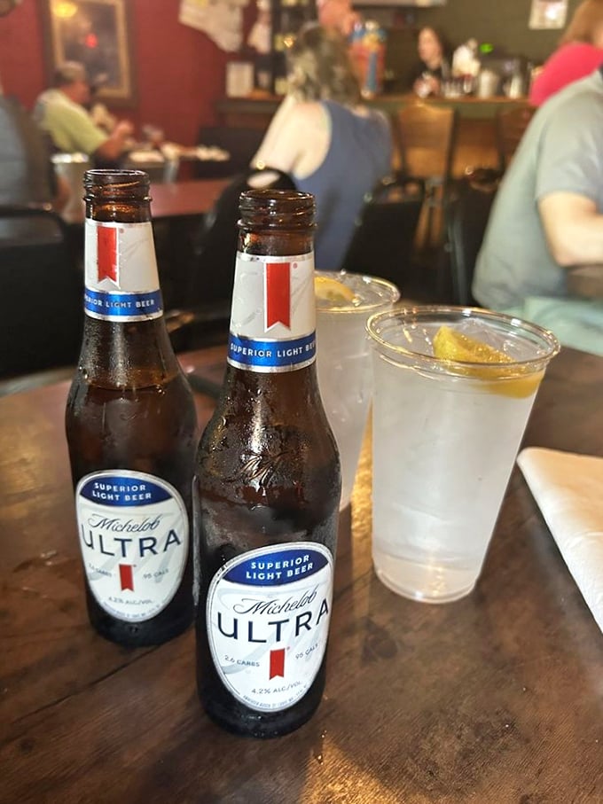 Cold Michelob Ultras and a sweating glass of something refreshing—because proper hydration while consuming legendary meat is just responsible adulting.