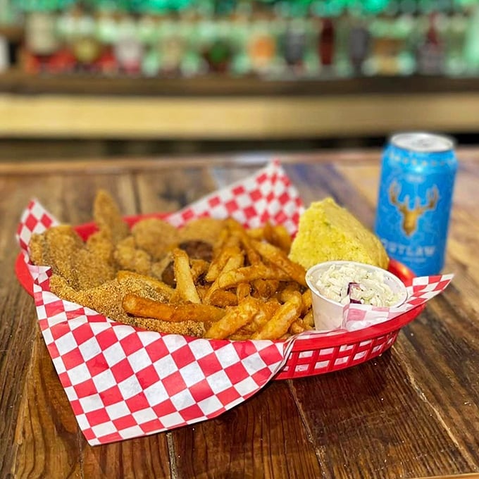 Crispy catfish with golden fries nestled beside cornbread and coleslaw—a Southern quartet performing a symphony of flavors on a red checkered stage.