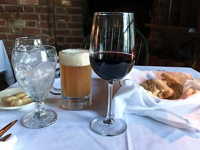 The holy trinity of dining pleasure: water to hydrate, beer to relax, wine to savor—all served against a backdrop of historic brick that's seen it all.
