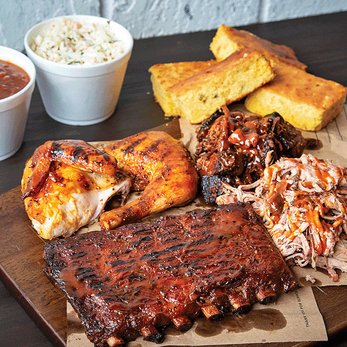 A barbecue board that belongs in the Louvre—golden cornbread, glistening ribs, and pulled pork arranged like edible art.