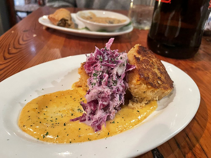 A golden crab cake perched on a pool of sunshine-yellow sauce with purple slaw—it's like edible modern art with Southern sensibilities.