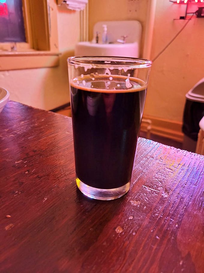 A proper pint of dark beer sitting on a worn wooden bar—sometimes the simplest pleasures are the ones we travel furthest to find.