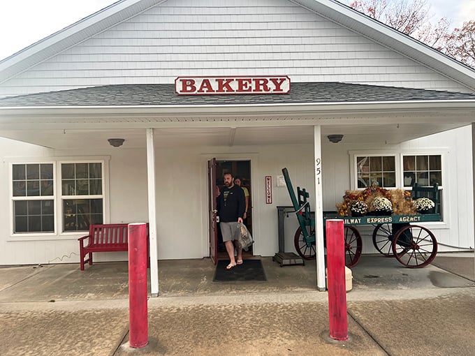 The quintessential country bakery facade—white clapboard, red accents, and a wooden wagon that silently promises carbs worth every mile of your journey.