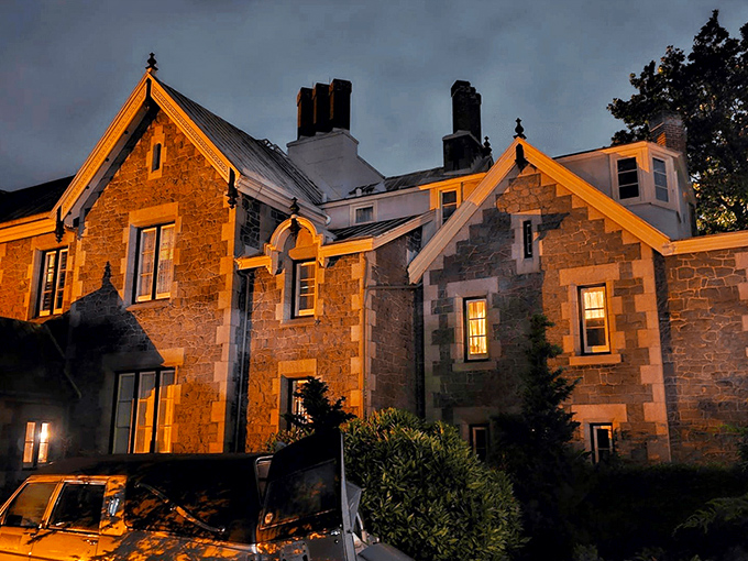 The mansion glows amber against the twilight sky, its stone façade and pointed gables silently whispering tales from another century. Like a Victorian ghost story come to life.