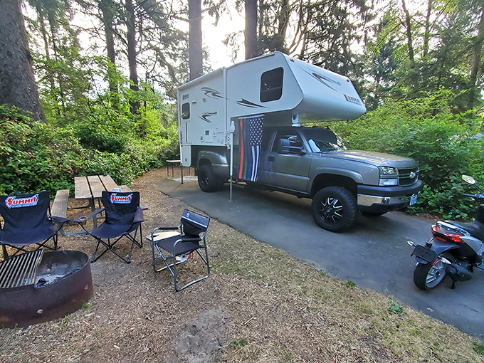 Camping nirvana achieved! A perfectly situated truck camper nestled among towering pines, with camp chairs awaiting stories around the fire ring.