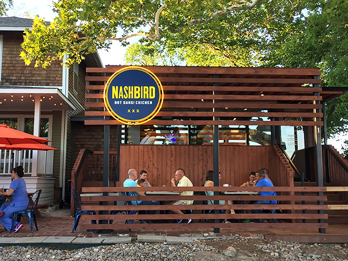 NASHBIRD's charming converted house exterior beckons with its wooden deck and bright signage—like a Southern porch that happens to serve life-changing chicken.