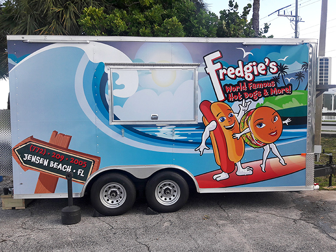 Paradise found: A cheerful blue food truck nestled among palm trees, where waterfront views come standard with every hot dog order.