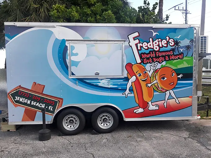 Paradise found: A cheerful blue food truck nestled among palm trees, where waterfront views come standard with every hot dog order.