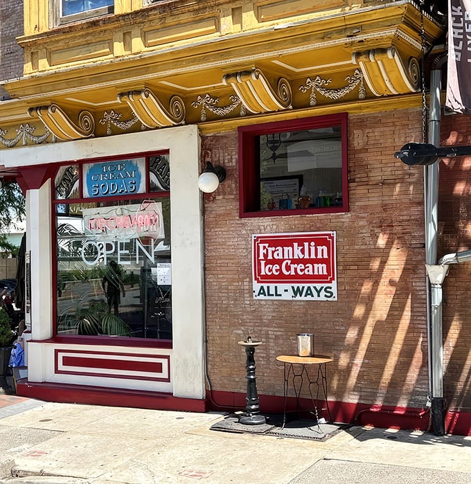 The storefront beckons like a time portal to ice cream's golden age—ornate yellow cornice, classic signage, and that brick facade promising sweet nostalgia inside.