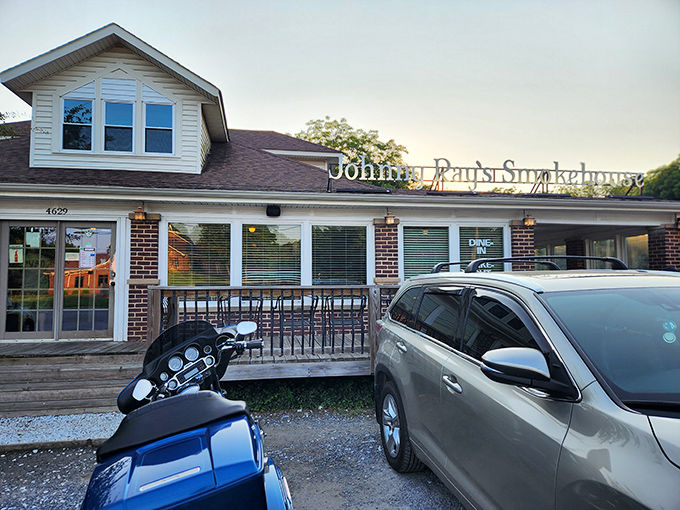 The welcoming glow of Johnny Ray's Smokehouse beckons hungry travelers with its homey brick exterior and cozy wooden deck—barbecue paradise found. 