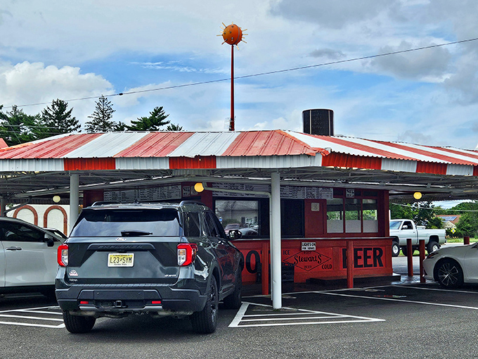 The iconic red and white striped canopy of Stewart's Drive-In stands like a time capsule on wheels, beckoning hungry travelers with promises of nostalgia and root beer.