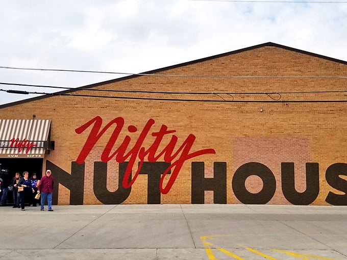 The brick facade of Nifty Nut House stands like a temple to temptation, its bold red script promising sweet adventures within.