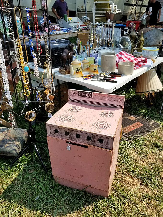 A pink vintage stove sits among costume jewelry and lampshades—someone's childhood kitchen appliance now waits for its second act as retro decor.
