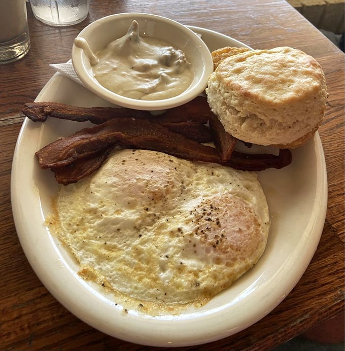 The platonic ideal of breakfast—a perfectly fried egg, bacon with architectural integrity, and a biscuit that would make your grandmother both proud and jealous.
