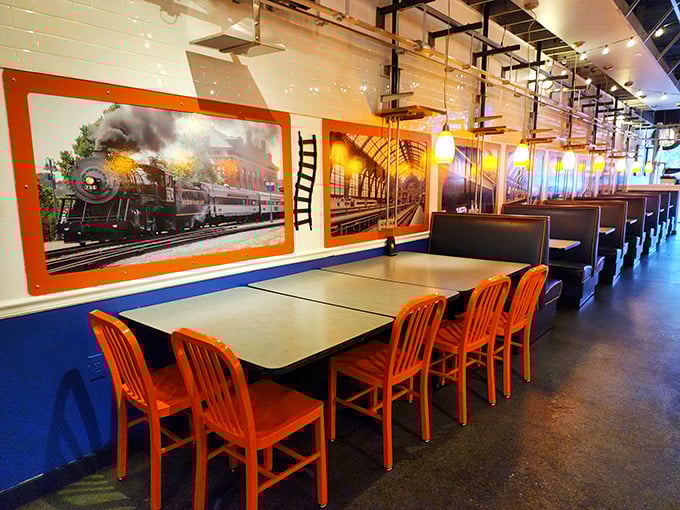 Bold orange chairs pop against blue walls adorned with vintage train artwork. The dining area feels like stepping into a stylish railway car from a more civilized era.