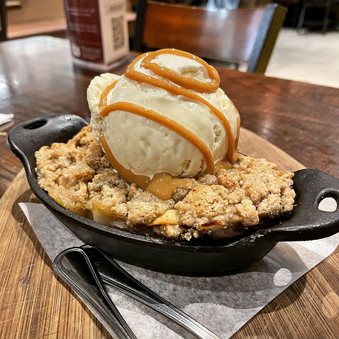 The apple crumble arrives sizzling in its own cast-iron skillet—ice cream melting into warm, buttery crumble like a delicious meteor hitting a tasty planet.