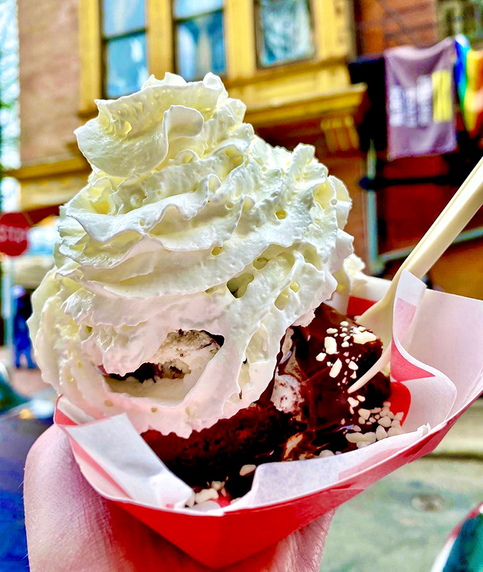This isn't just dessert, it's architecture—whipped cream peaks towering over red velvet valleys in a paper boat of pure bliss.