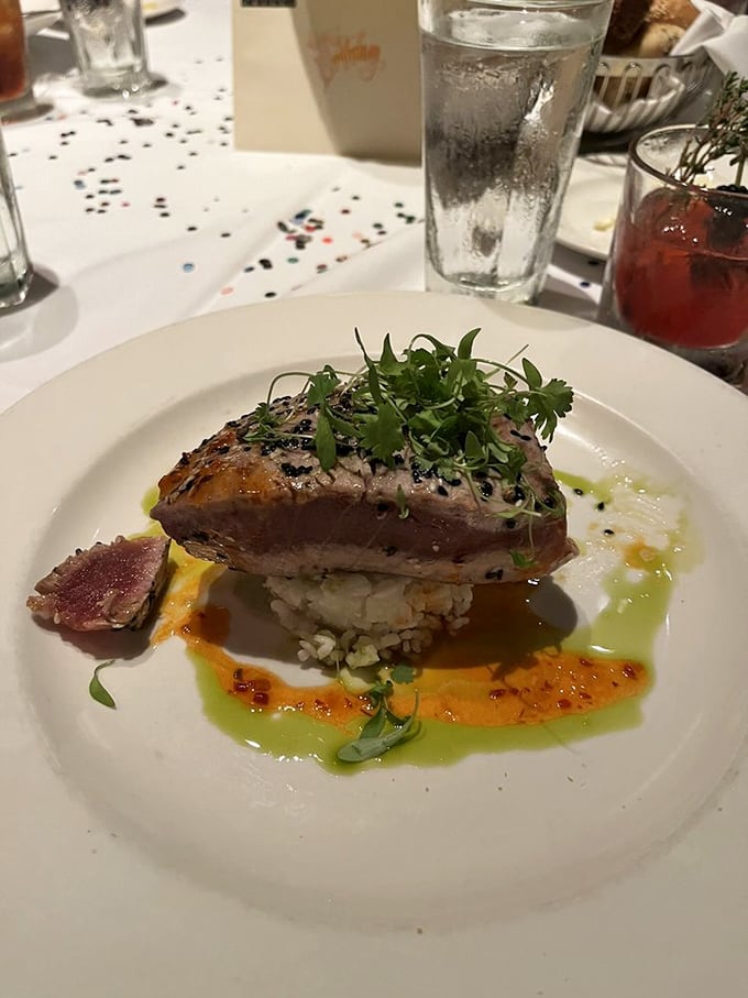 A pink-centered tuna steak perched regally atop its throne of rice, surrounded by colorful sauce swooshes like an edible modern art installation.