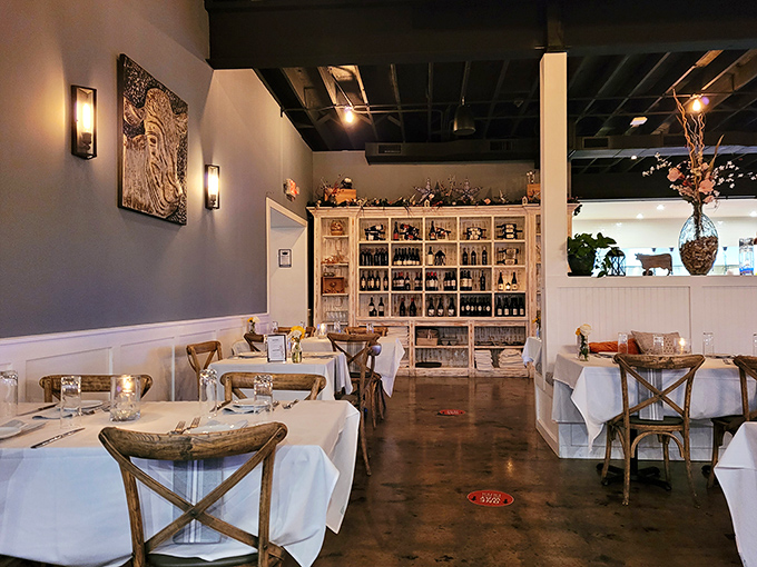 Elegant simplicity defines the dining room, where white tablecloths meet rustic wooden chairs. The impressive wine display isn't just decoration—it's foreshadowing for the perfect pairing adventure ahead.
